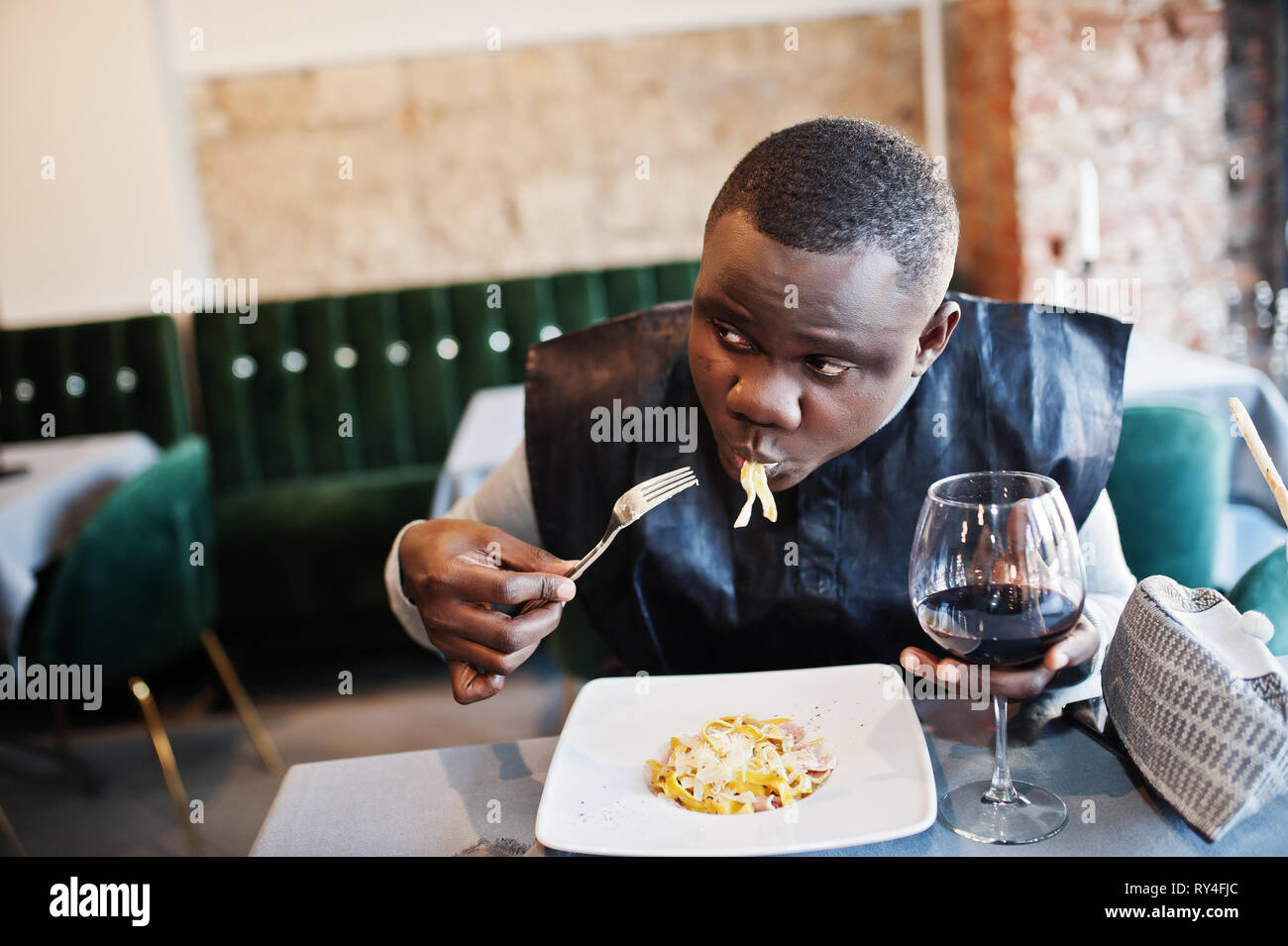 African man in black traditional clothes sitting at restaurant and eat ...