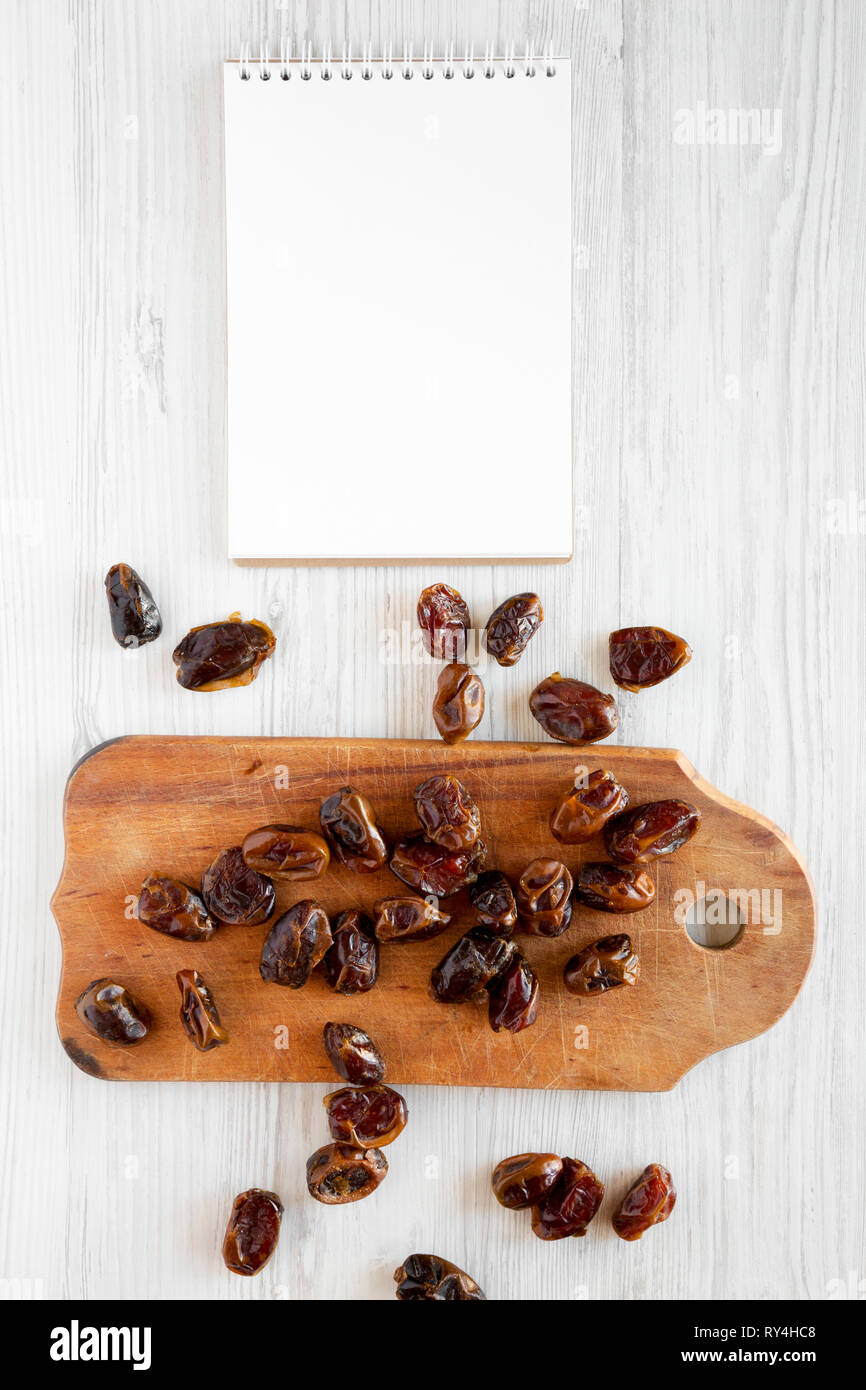 Top view, dried dates on rustic wooden board, blank notepad on a white ...
