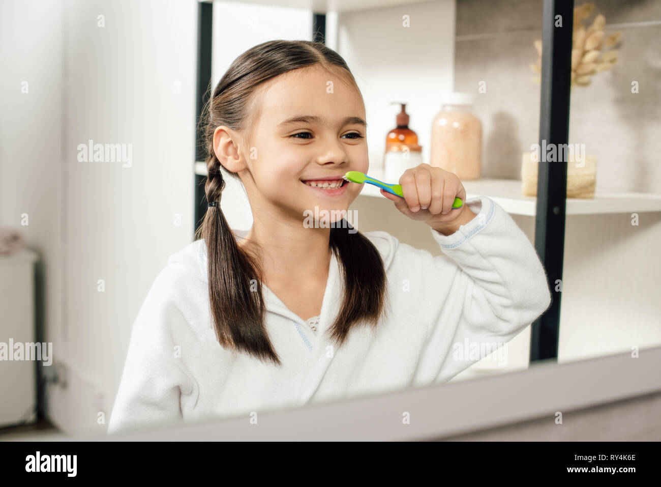 selective focus of child in white bathrobe looking to mirror and ...