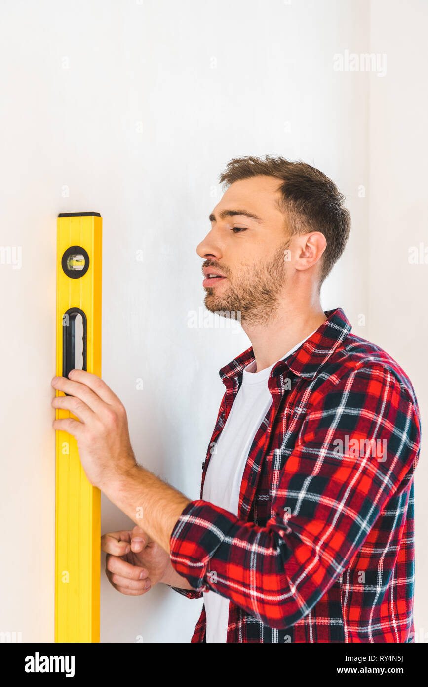 handsome man holding measuring level while measuring wall at home Stock ...