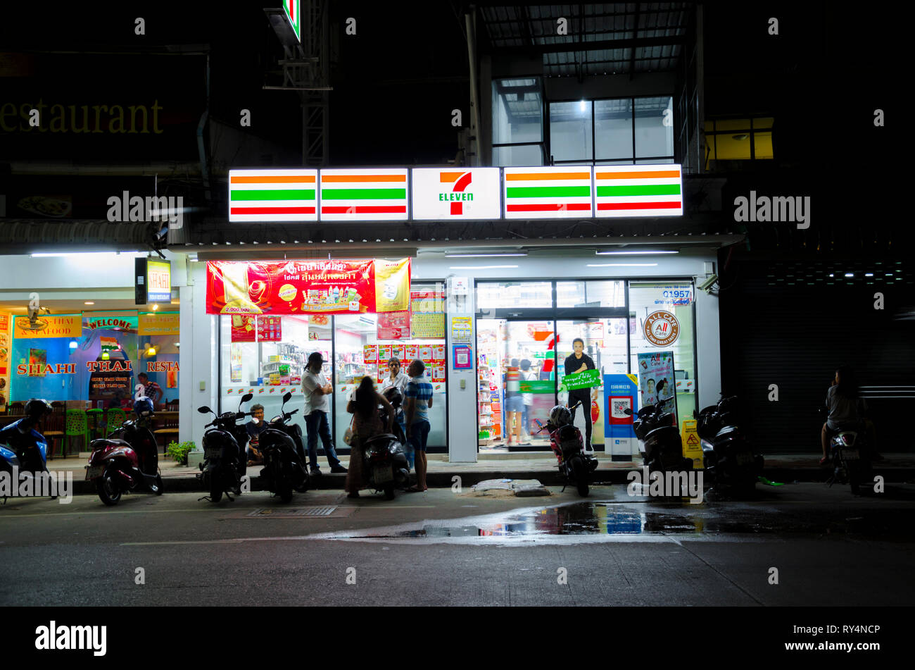 Pattaya, Thailand - February 15, 2019: Nighttime street scene with pedestrians outside a 7 ...