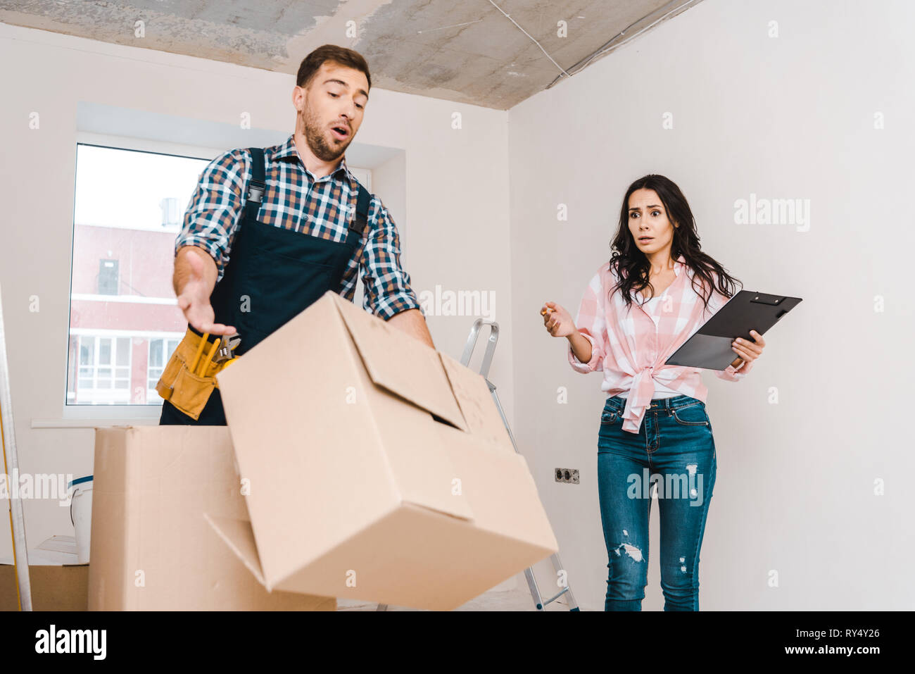 surprised woman looking at falling box near handyman Stock Photo - Alamy