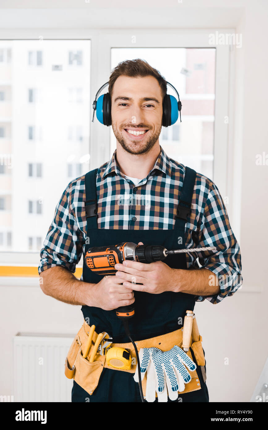 handsome handyman smiling while holding drill in hands Stock Photo - Alamy