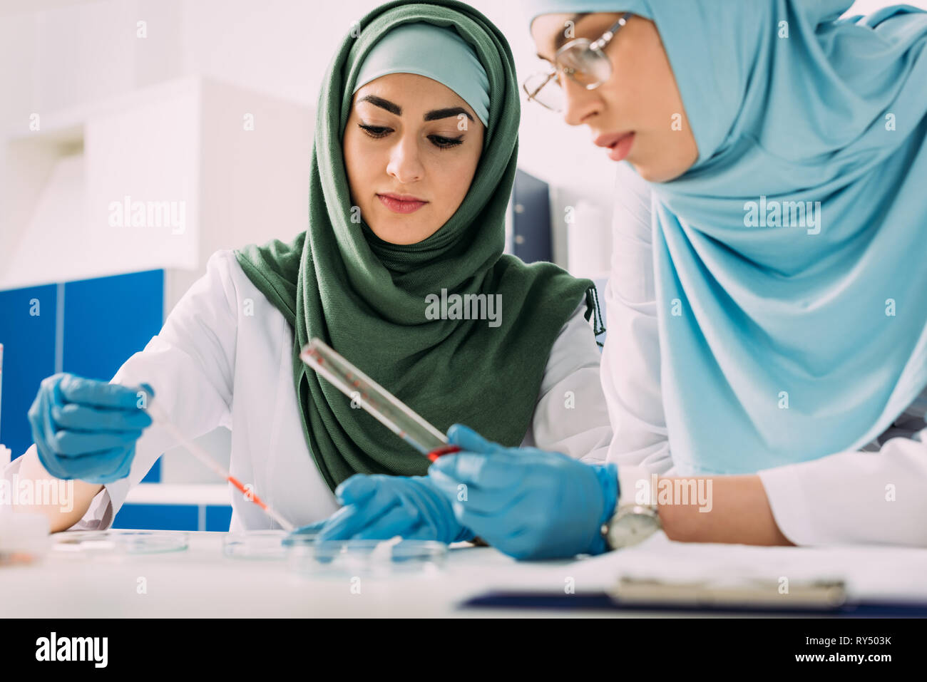 focused female muslim scientists holding pipette and glass test tube ...