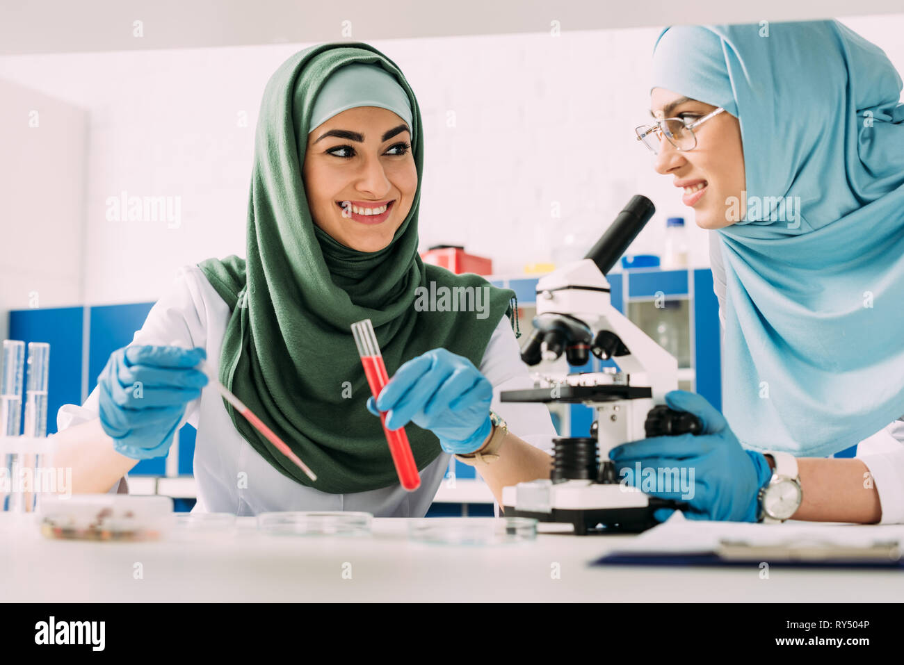 female muslim scientists with glass tube, pipette and microscope during ...