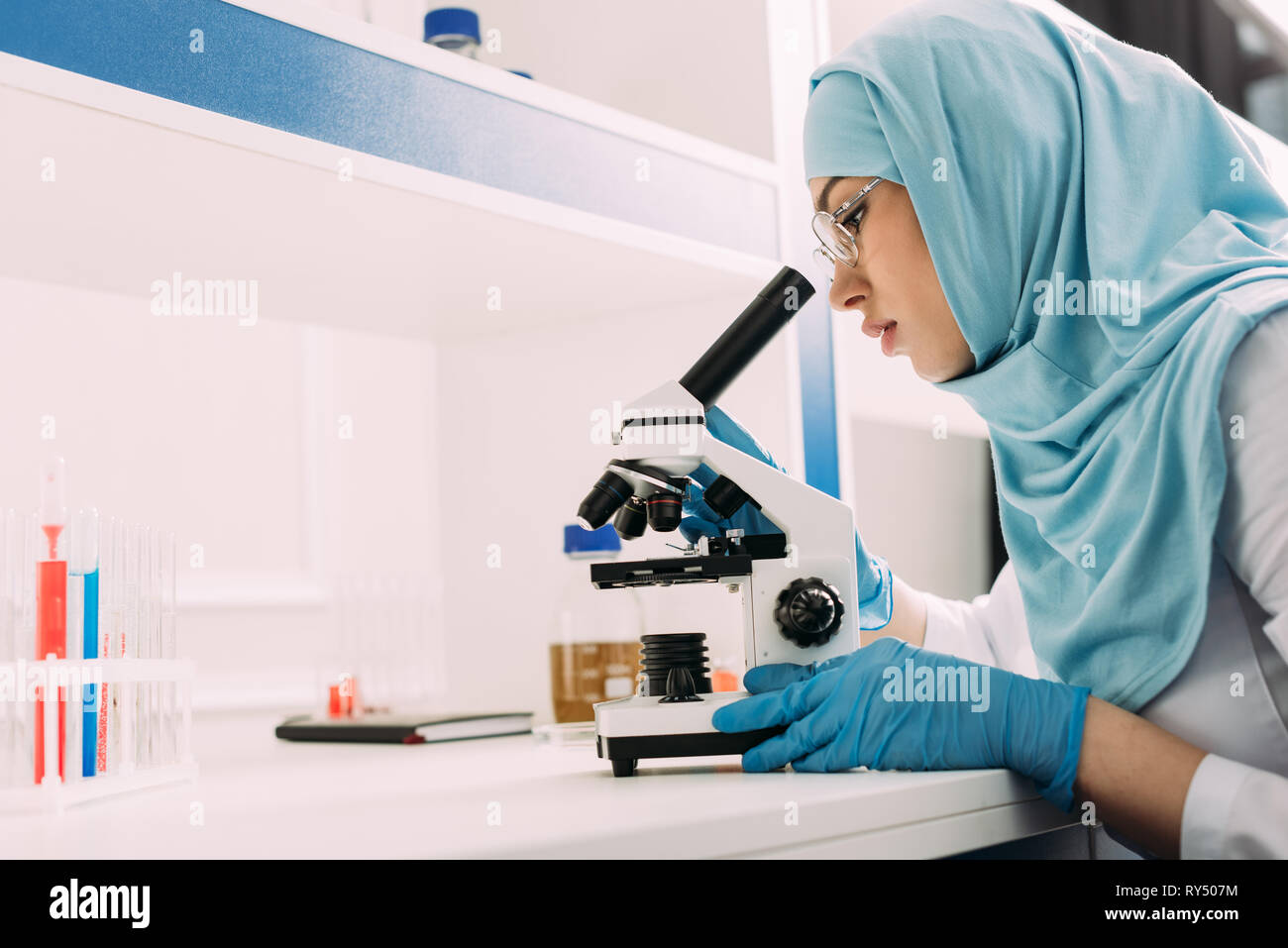 female muslim scientist looking through microscope during experiment in ...