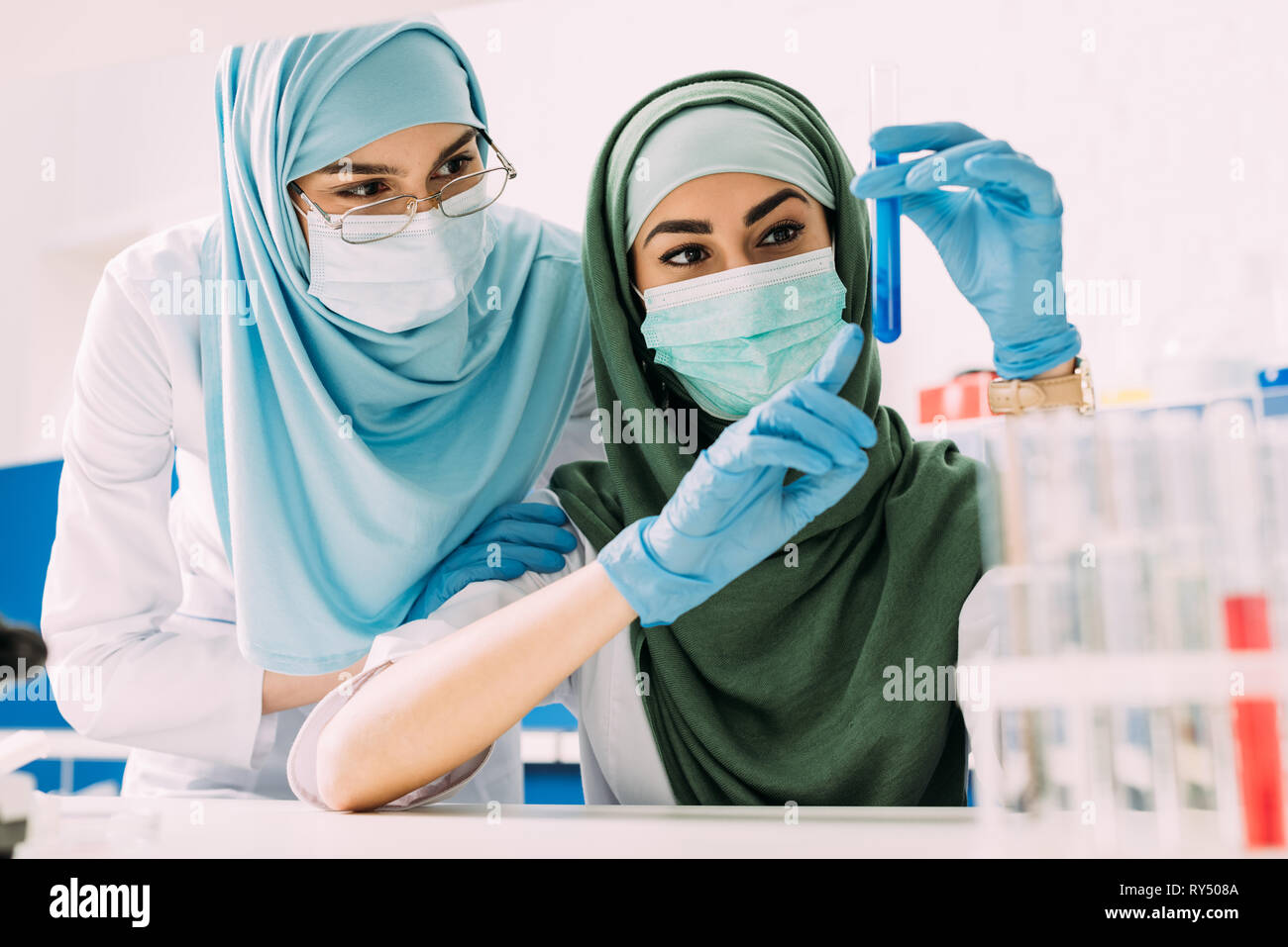 female muslim scientists in medical masks pointing with finger at glass ...