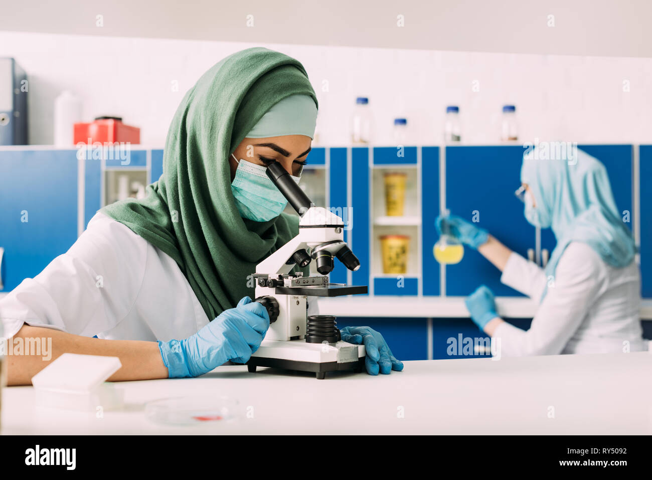 female muslim scientist looking through microscope during experiment ...