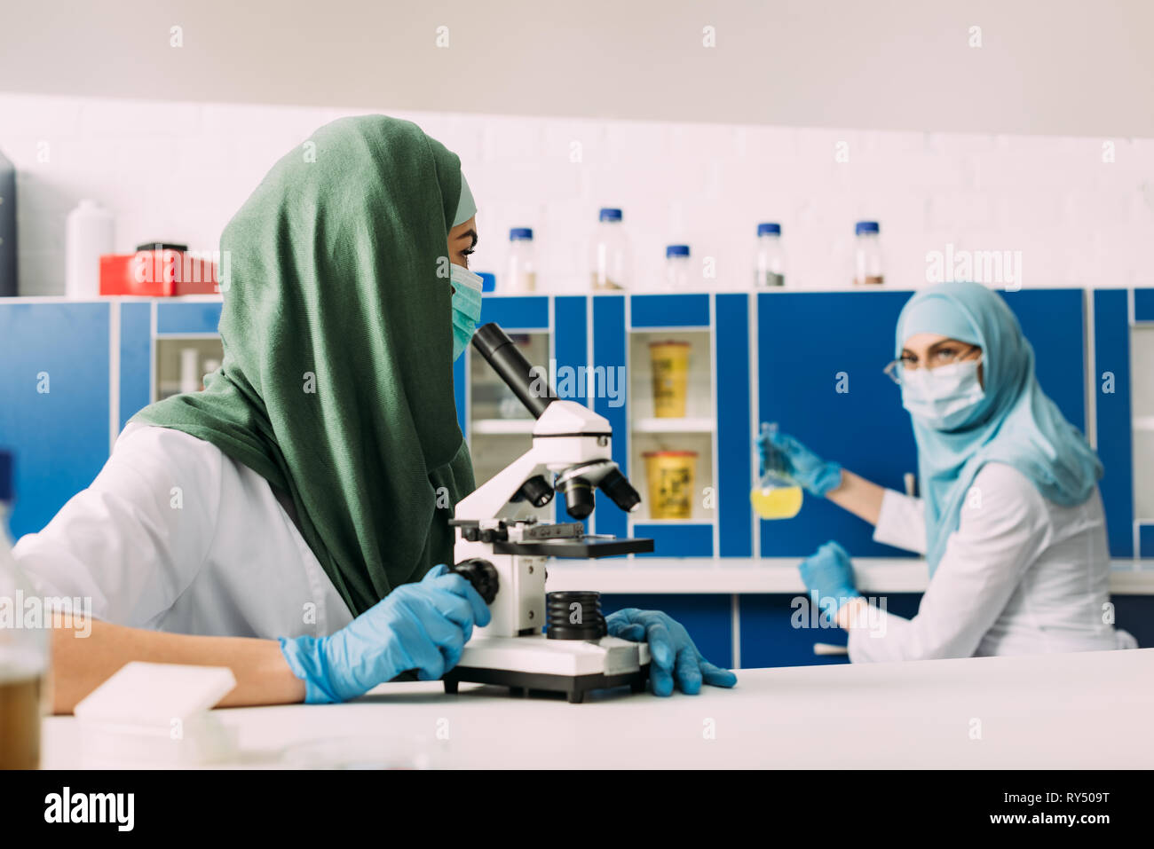 female muslim scientist using microscope during experiment with ...