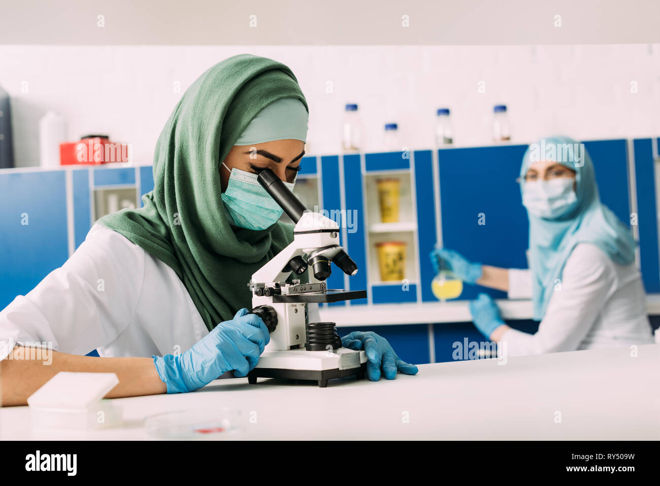 female muslim scientist looking through microscope during experiment ...
