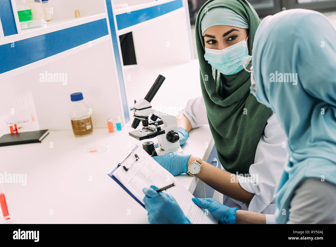 female muslim scientists in hijab using microscope and clipboard during ...