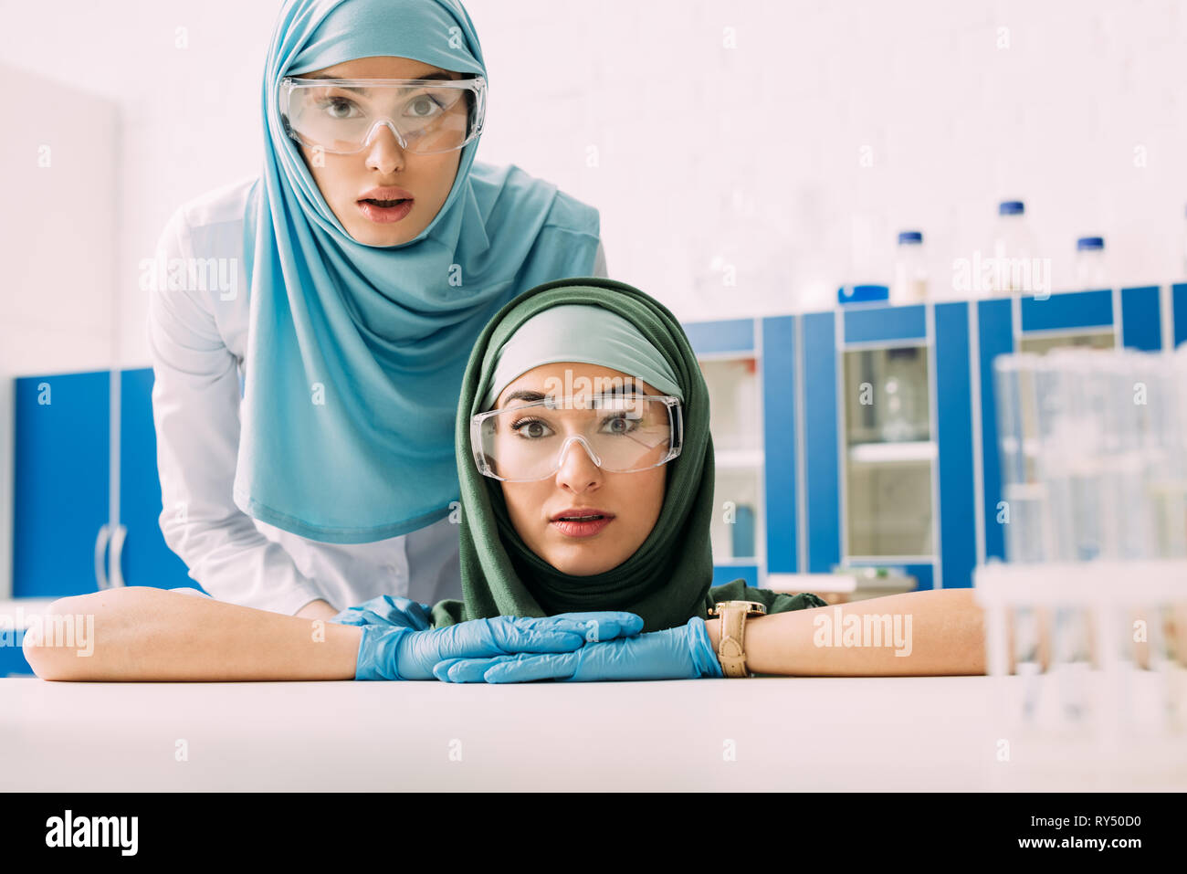 female muslim chemists in protective goggles and hijab looking at camera in laboratory Stock ...
