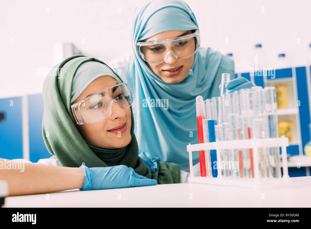 female muslim scientists in goggles looking at reagents in glass test ...