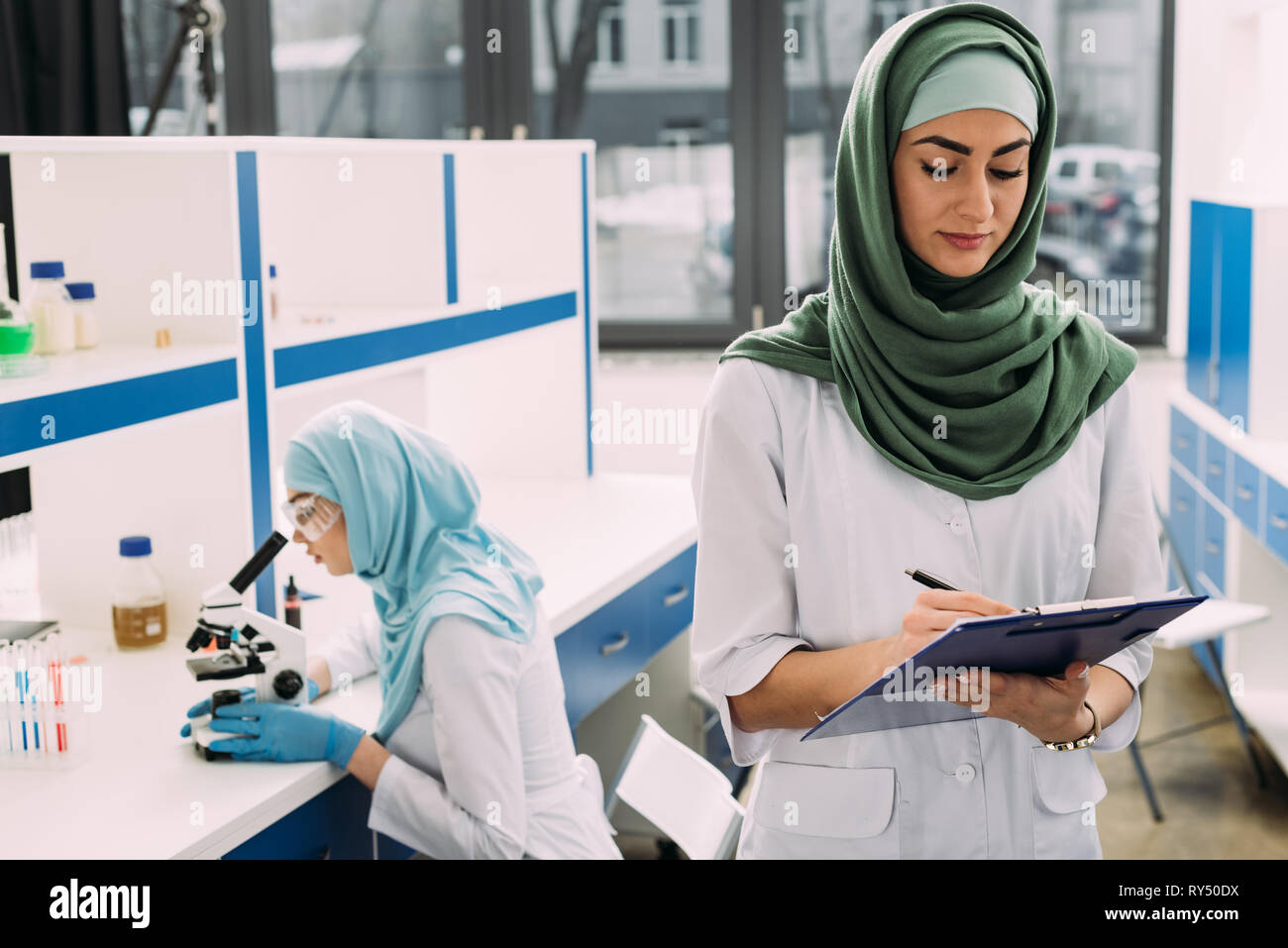 concentrated female muslim scientists using microscope and writing in ...
