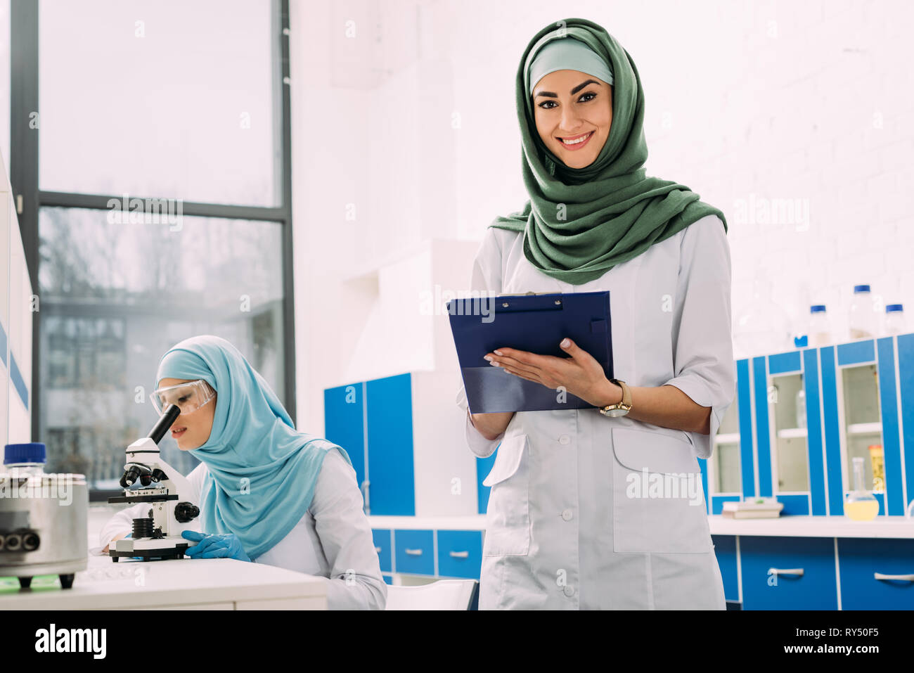 female muslim scientists using microscope and clipboard during ...