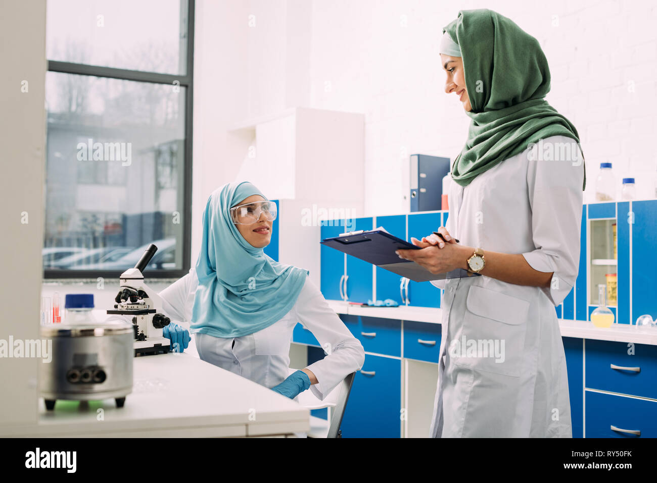 female muslim scientists using microscope and clipboard during ...