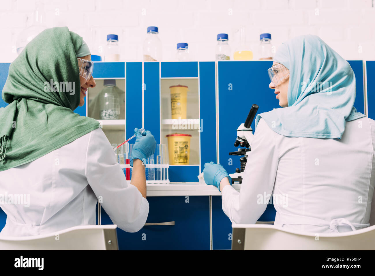 back view of female muslim scientists using pipette and microscope in ...