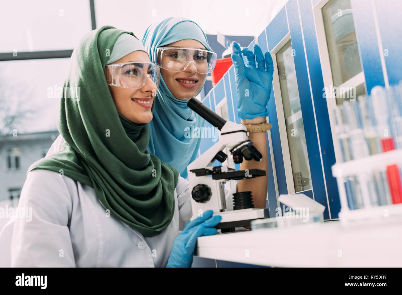 smiling female muslim scientists with microscope and glass sample ...