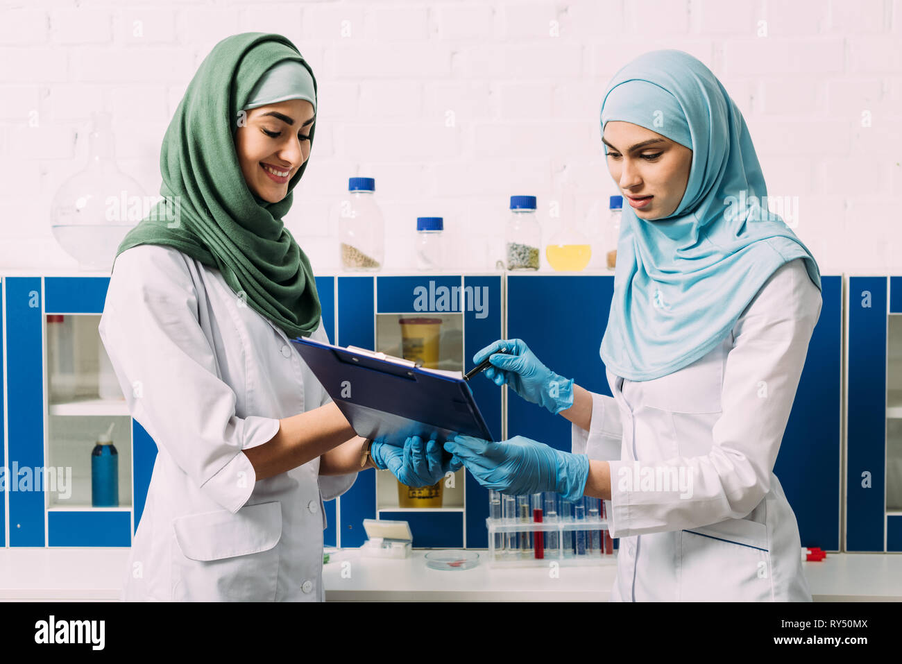 female muslim scientists in hijab holding clipboard during experiment ...