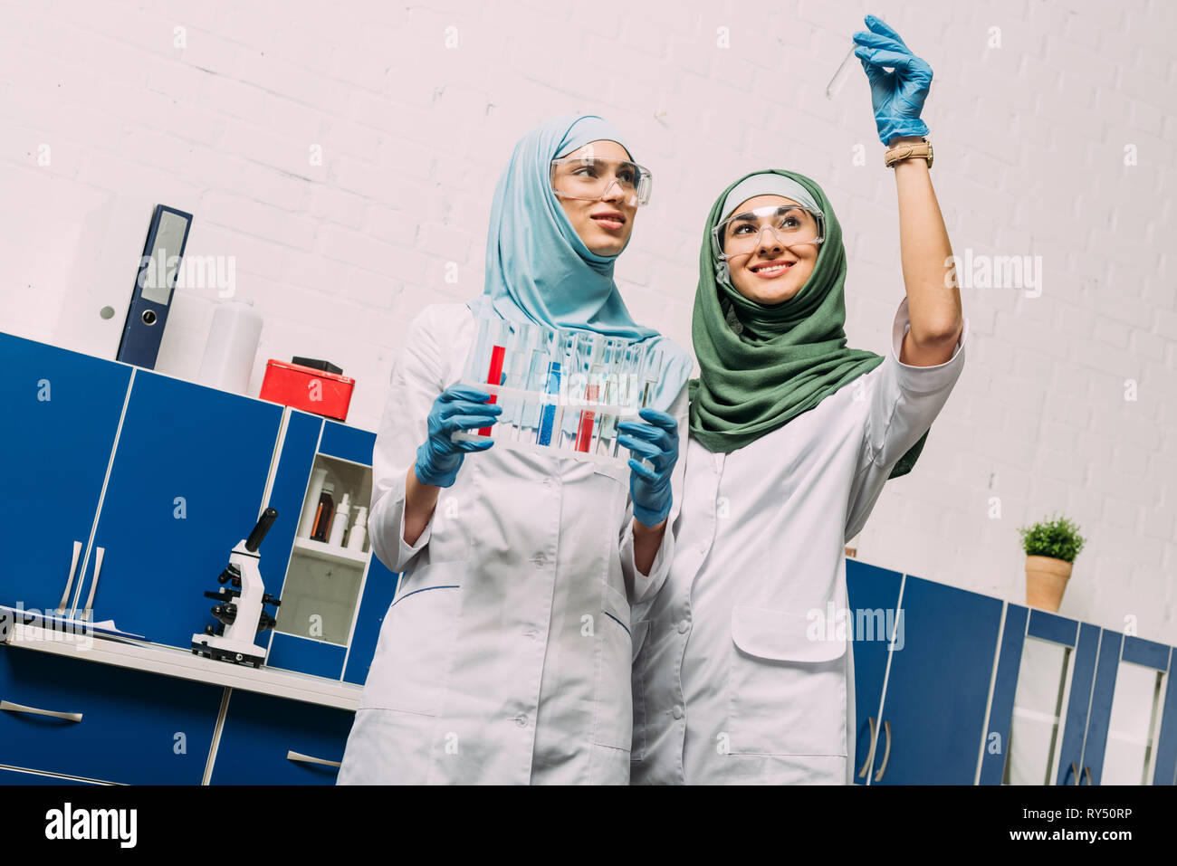 female muslim scientists in hijab holding test tubes with reagents ...