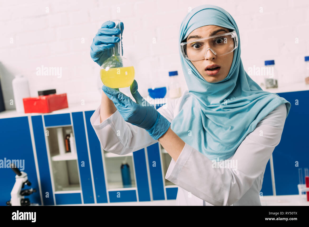 shocked female muslim scientist looking at camera and holding flask ...