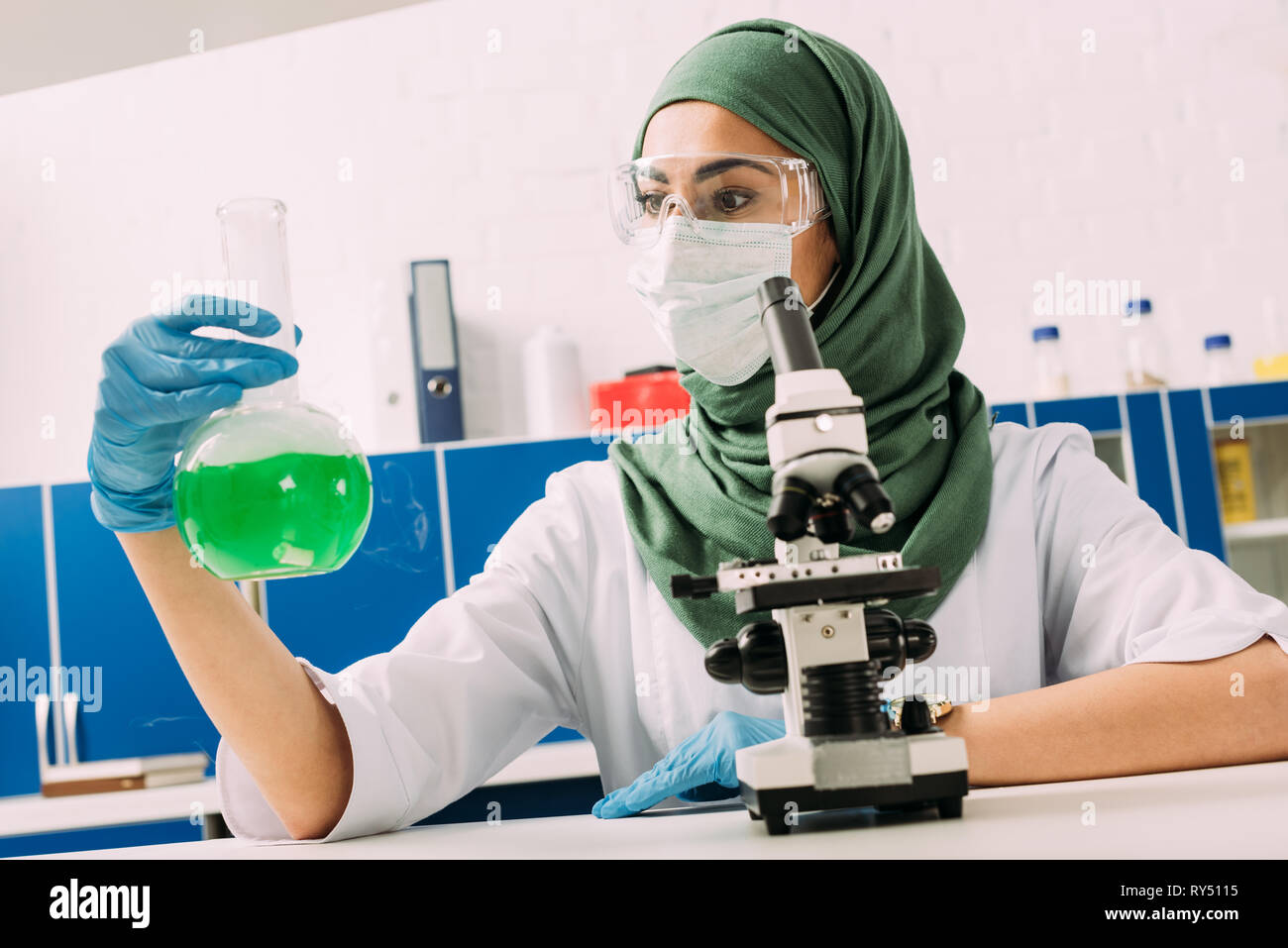 female muslim scientist sitting at table with microscope and holding ...