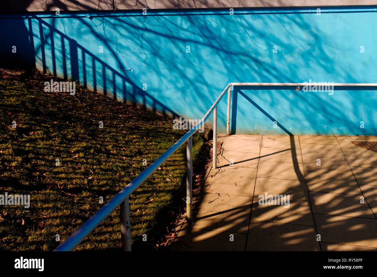 A galvanized hand rail joins on to a sky blue wall bathed in sunshine ...