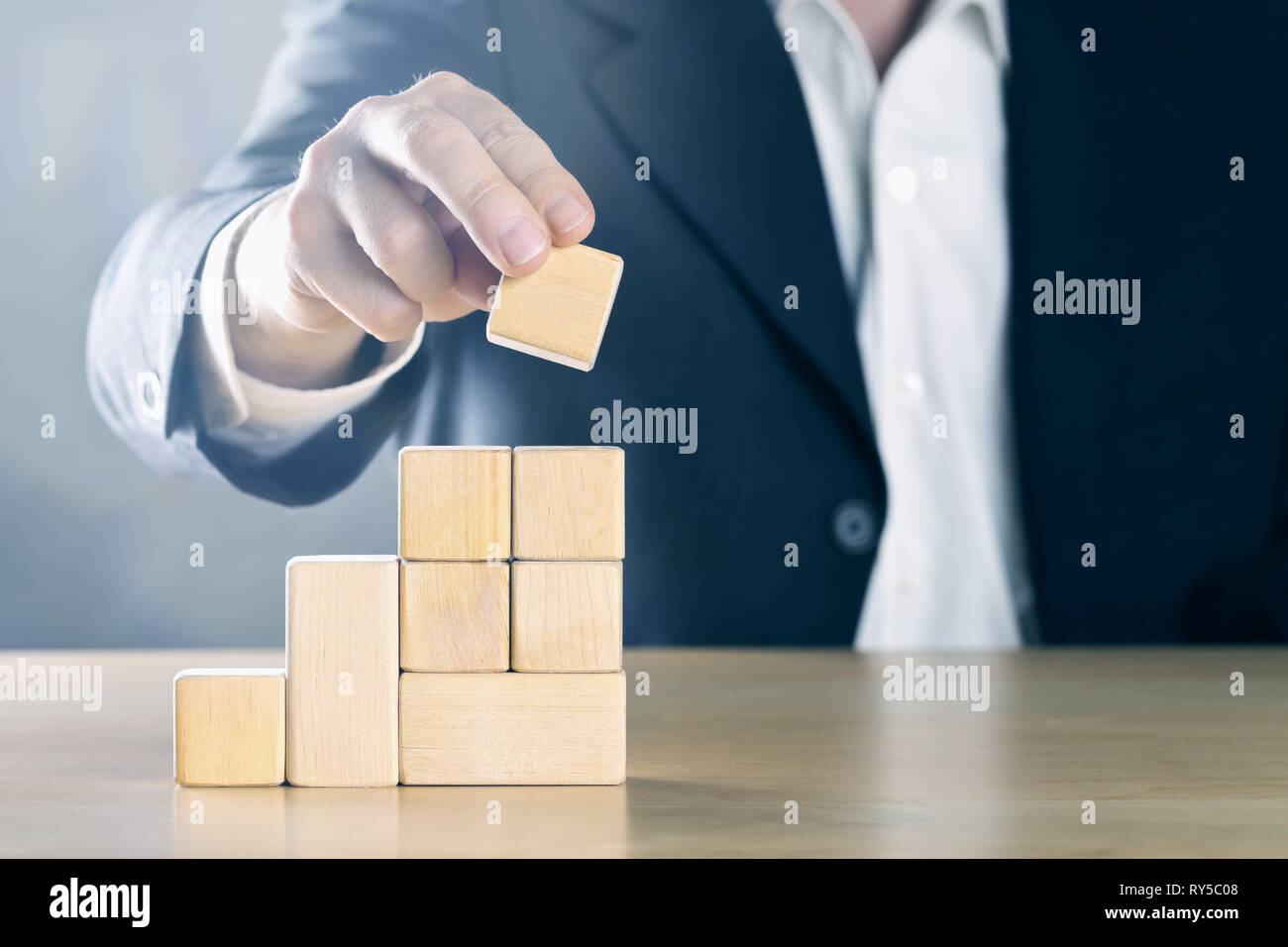 Business man puts next stone on career ladder made from wooden blocks ...