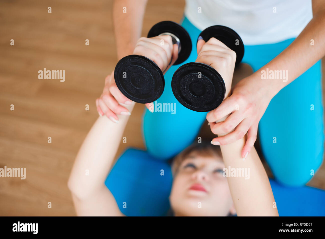 Personal coach helping woman to do exercises with dumbbells in gym ...
