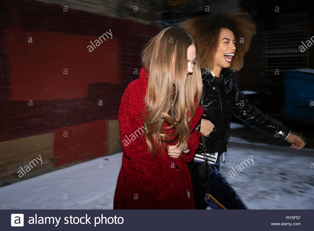 Laughing women friends walking arm in arm on snowy urban street Stock ...