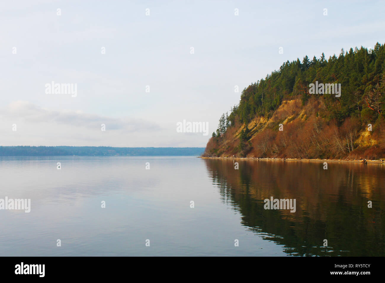 Calm water in the Puget Sound with a cliff in Joemma Beach State Park ...