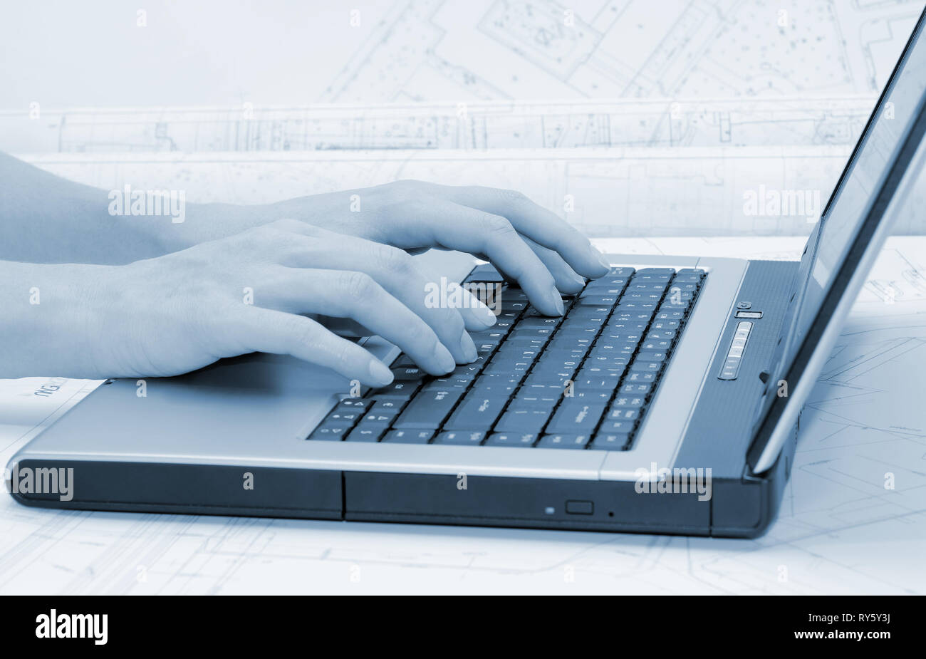 Female hands on laptop keyboard. Architectural plans in background ...