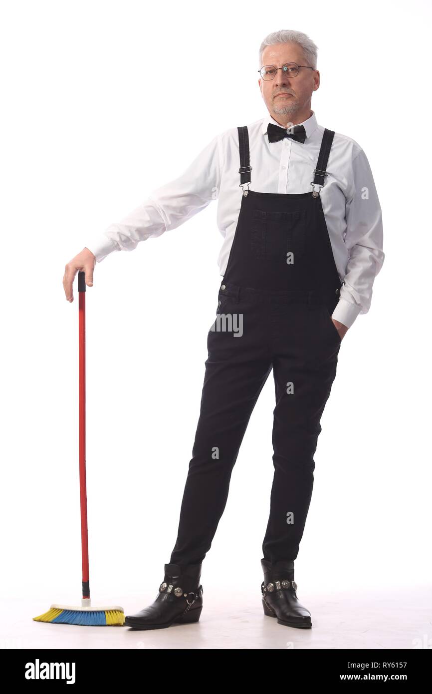 Gray-haired cleaner, janitor in a black jumpsuit with a mop and dustpan ...