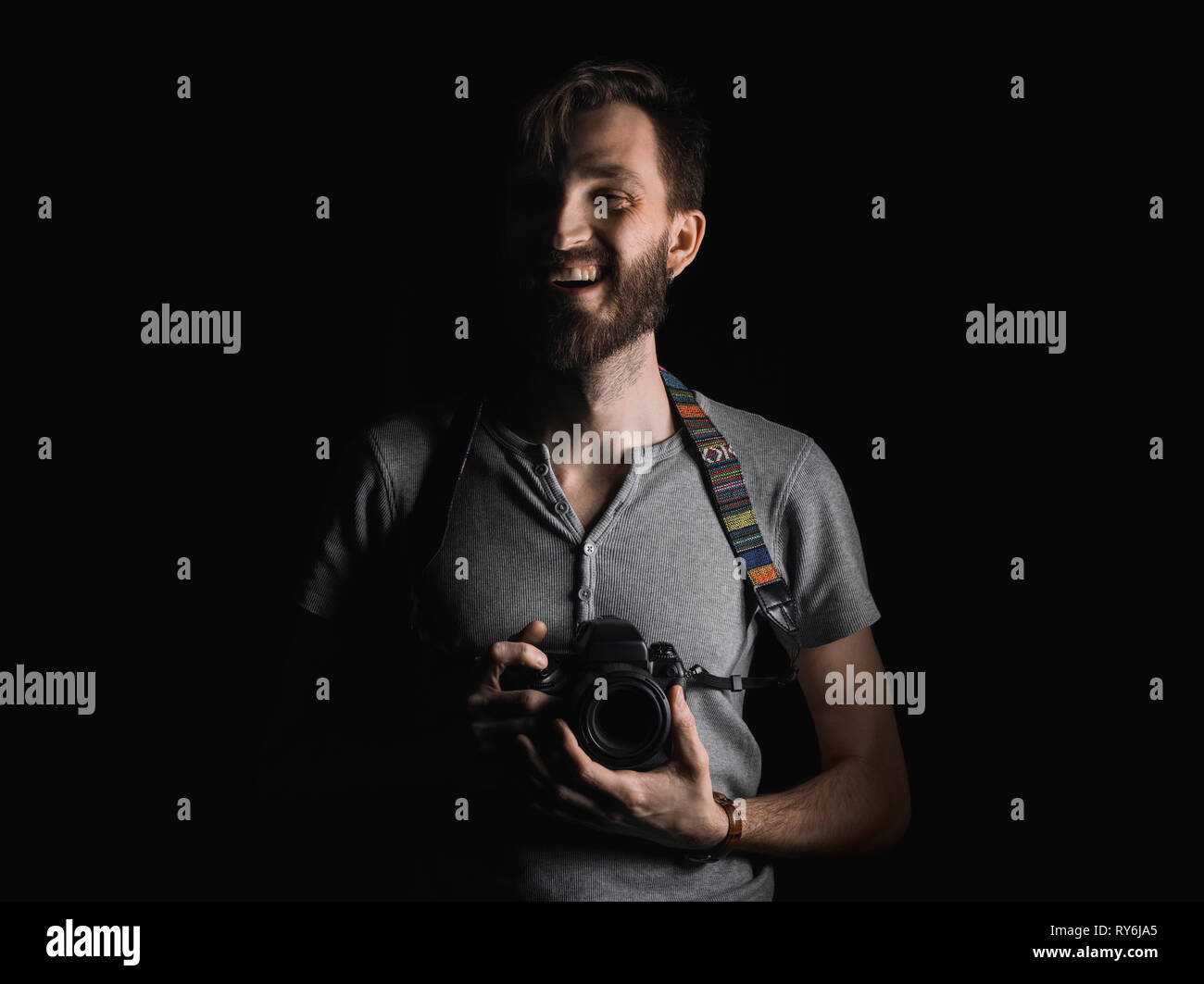 Happy man with camera looking away while standing against black ...