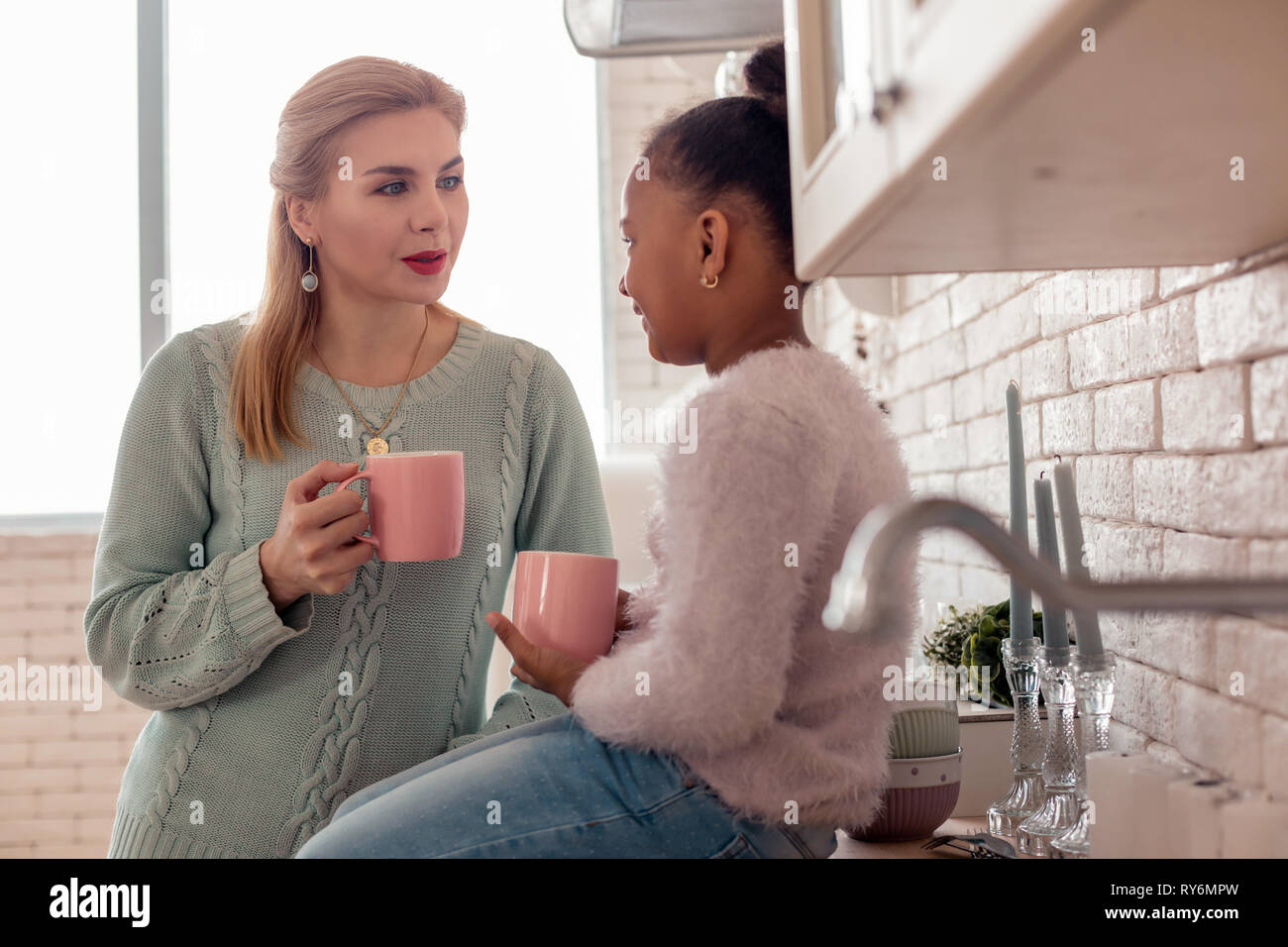 Caring mother wearing blue sweater talking to her lovely cute girl ...
