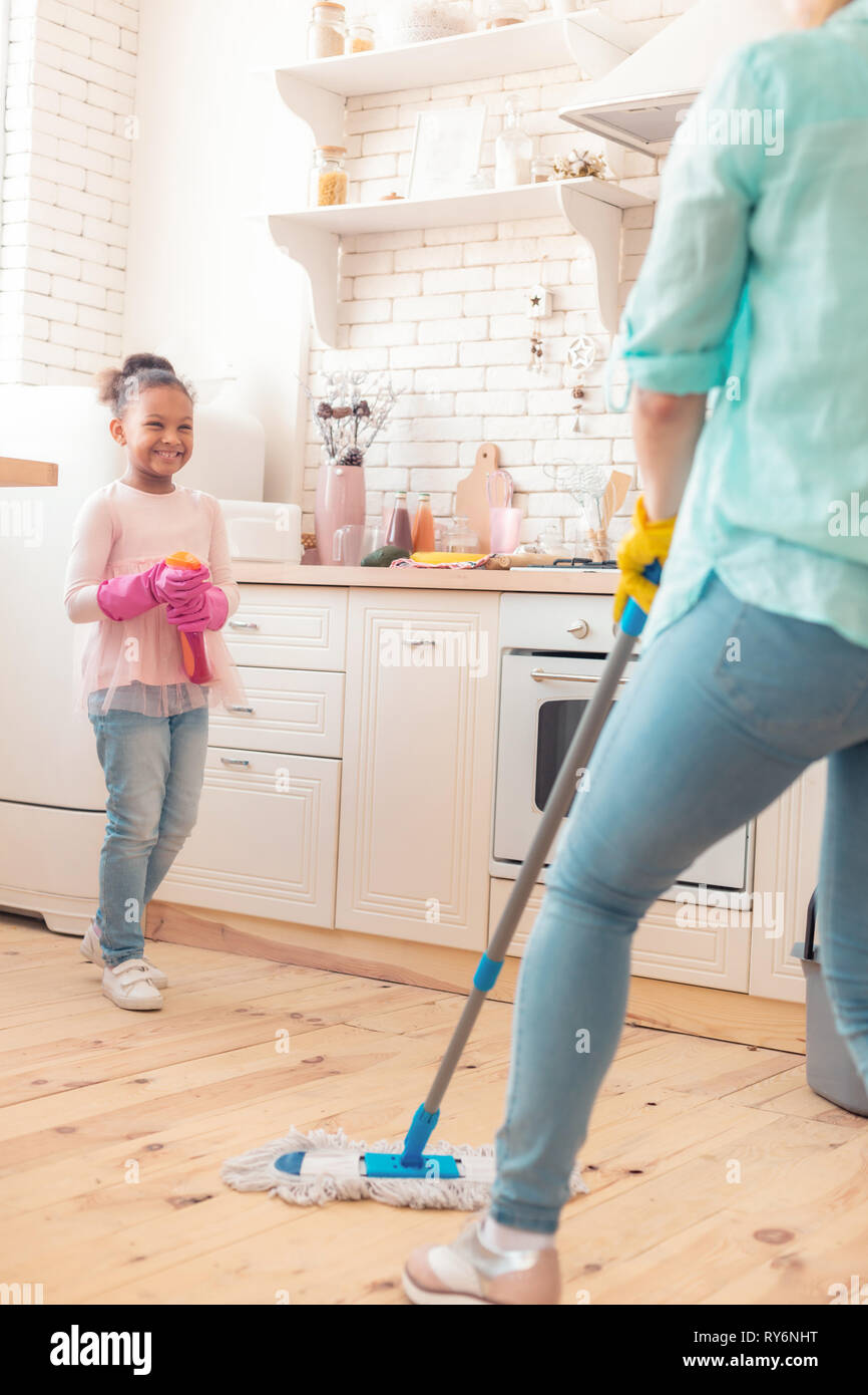Cute beaming girl looking at her mother mopping the floor Stock Photo ...