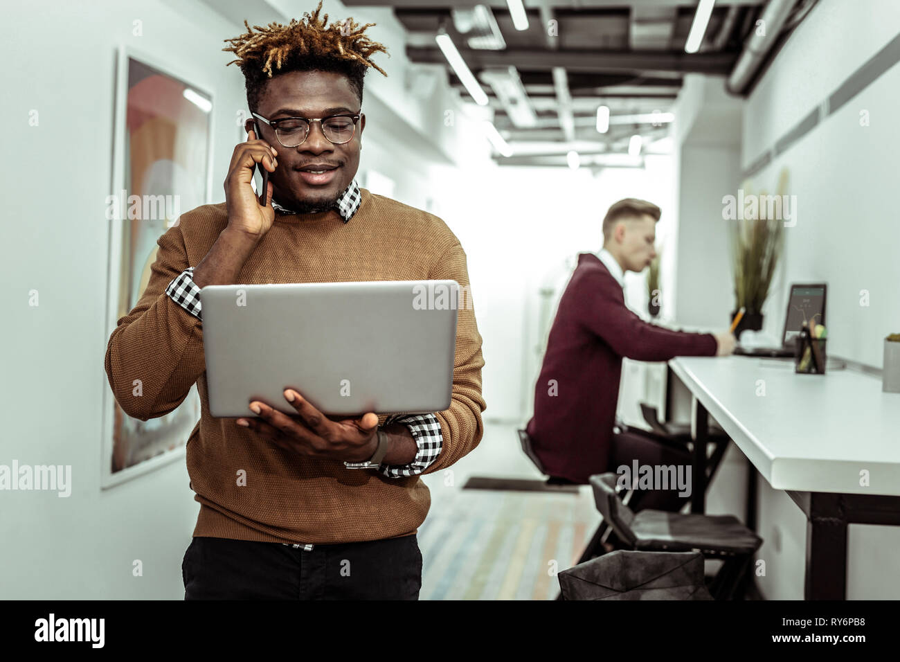 Concentrated dark-skinned guy answering on phone call while carrying ...