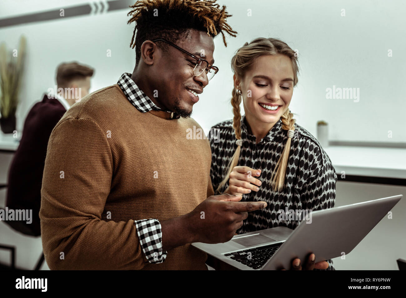 Cheerful guy with dreadlocks carrying laptop and explaining information ...