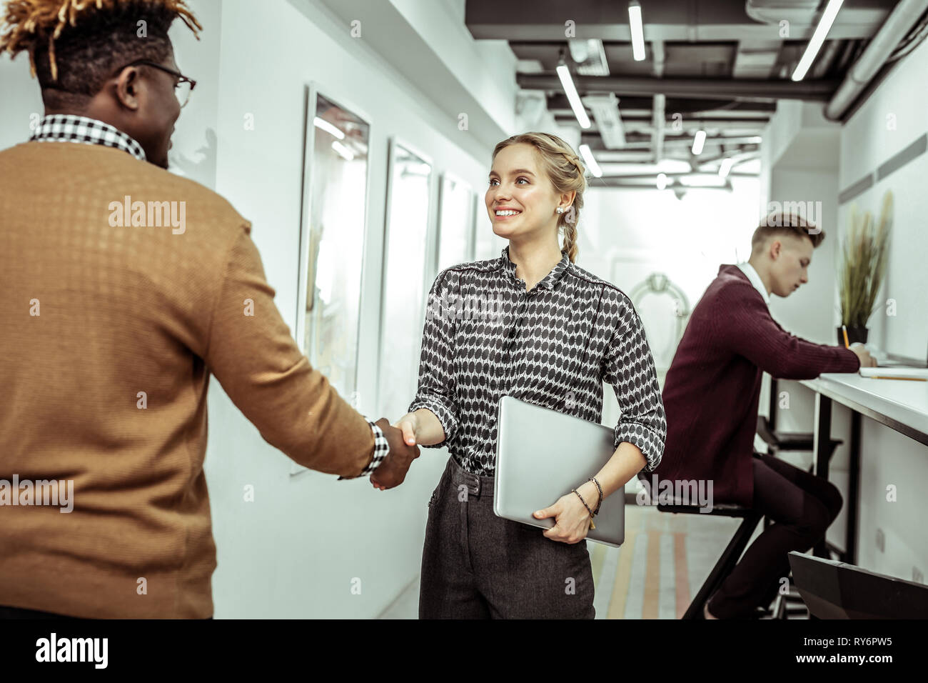 Cheerful young lady in black and white shirt greeting new workmate ...