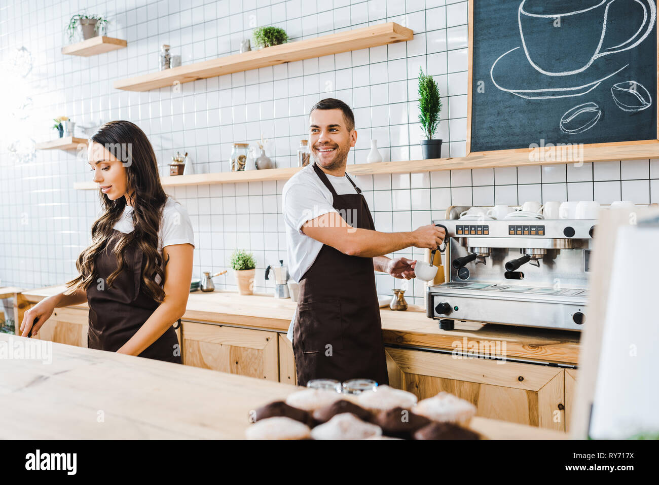barista making coffee and smiling wile attractive cashier working ...