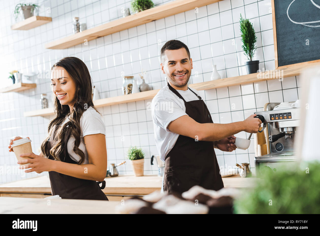 brunette attractive cashier holding paper cup wile barista making ...