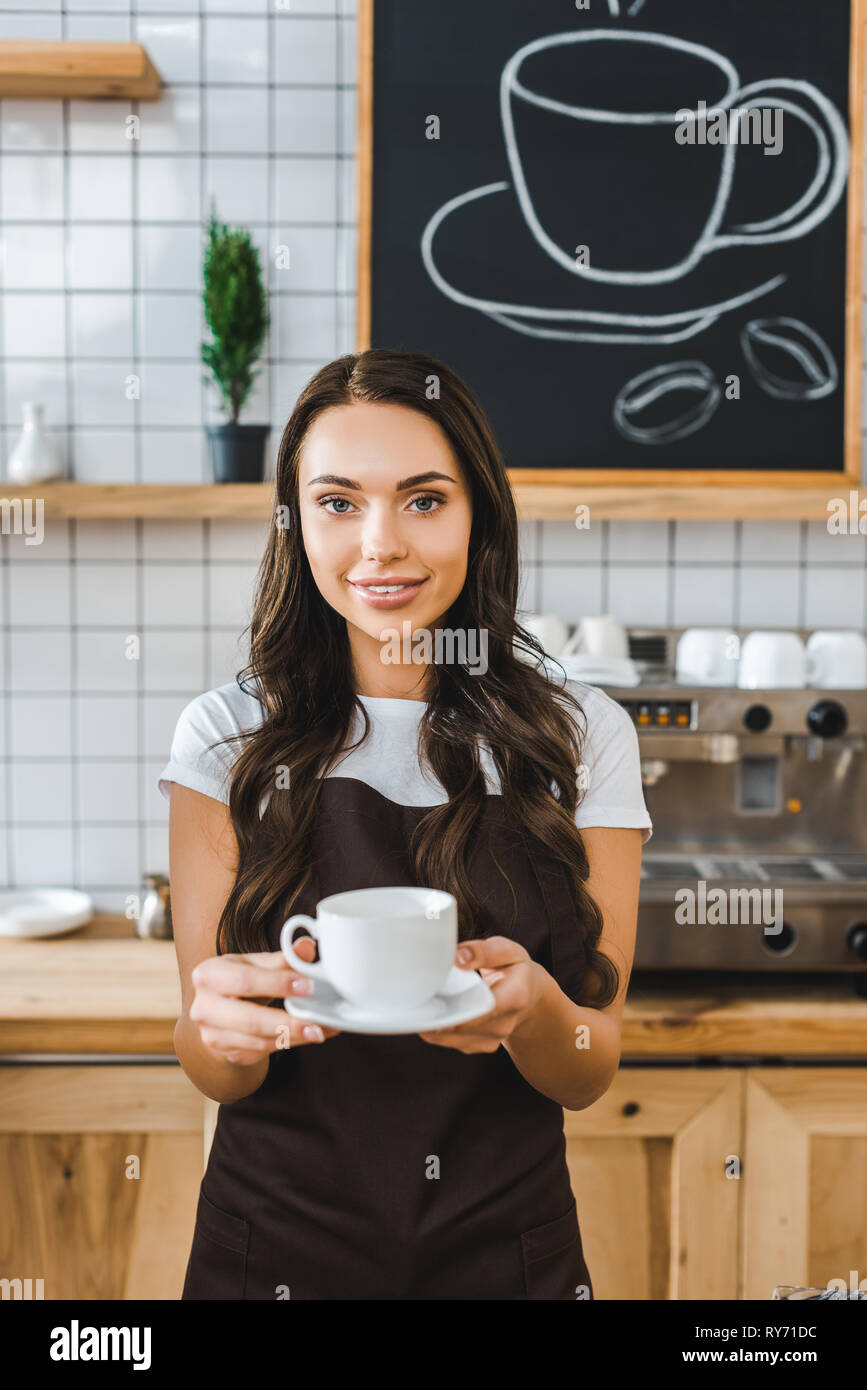 attractive barista in brown apron holding cup and saucer in coffee ...