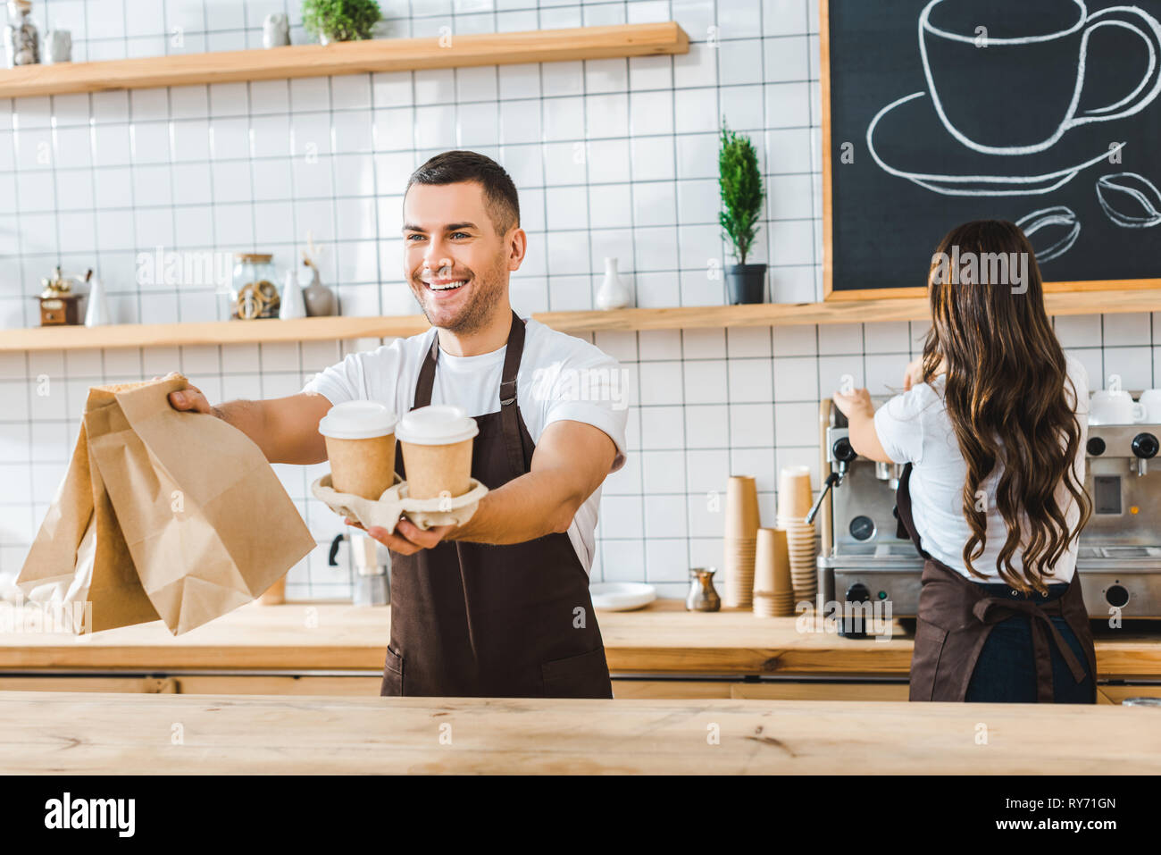 handsome cashier holding paper cups and bags wile attractive brunette ...