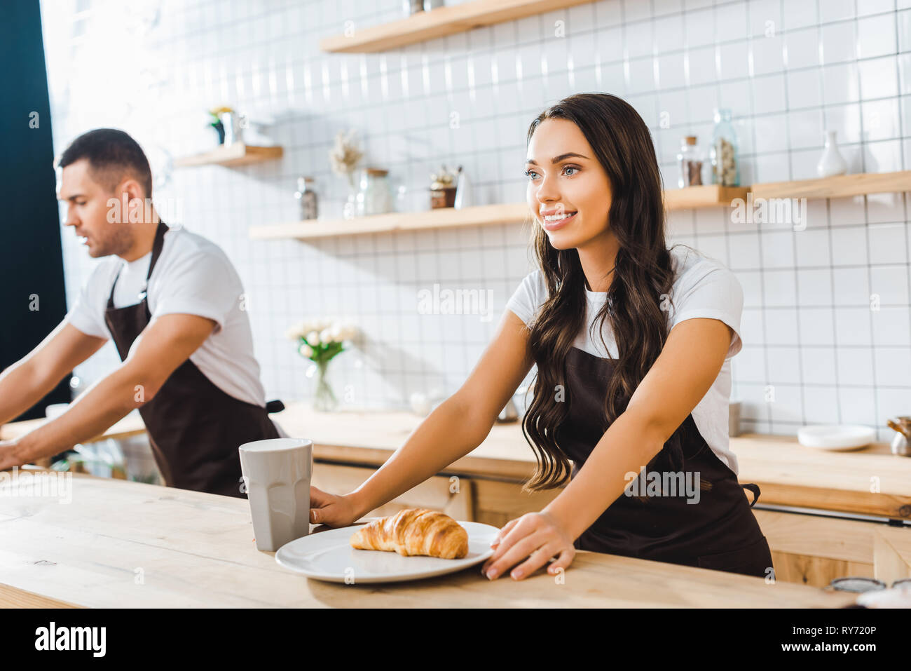 attractive cashier standing behind bar counter with cup, plate and ...