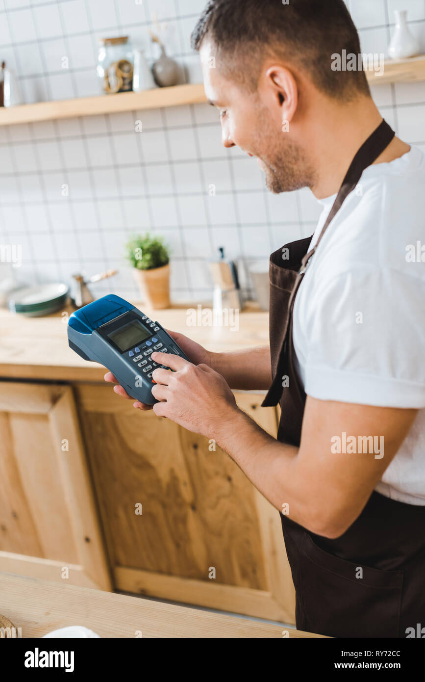 cashier standing in brown apron near bar counter and holding blue ...