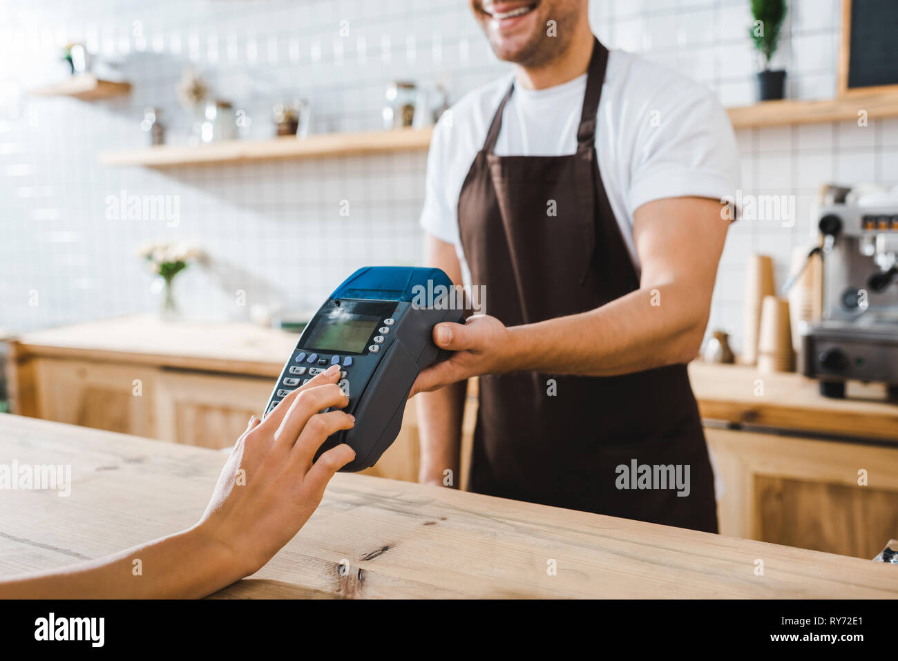 cropped view of cashier standing near bar counter and holding terminal ...
