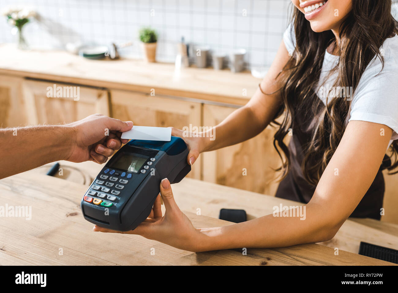 cropped view of cashier standing near bar counter in brown apron and ...