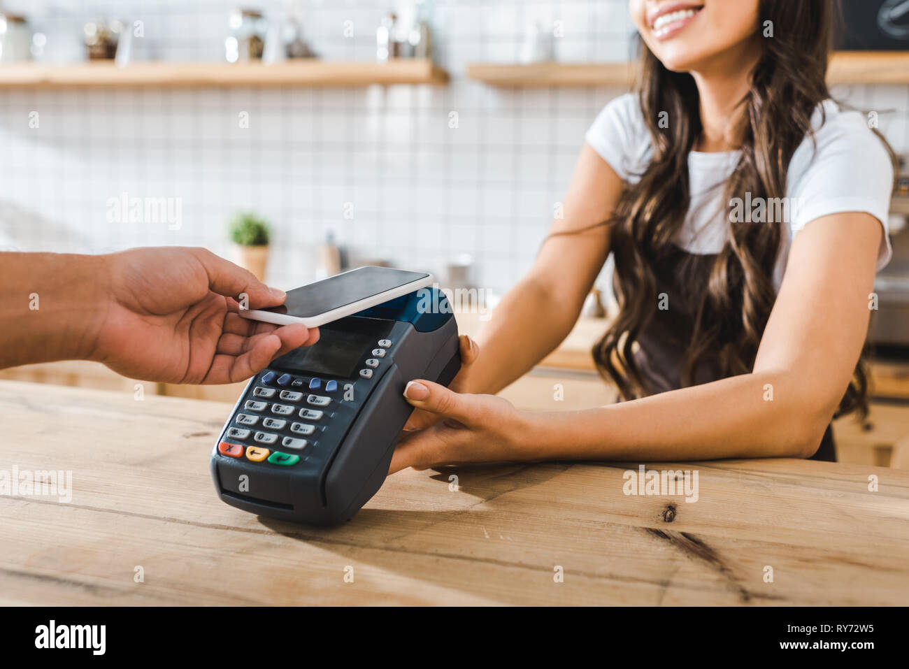 cropped view of cashier standing near bar counter in brown apron and ...