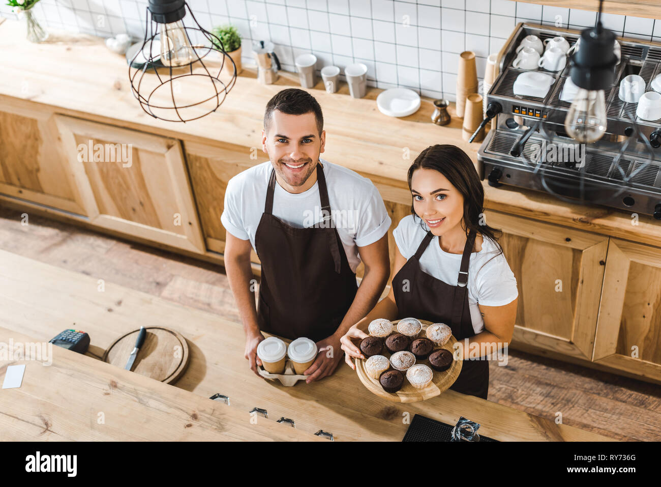 attractive cashier with cupcakes and handsome barista with paper cups ...