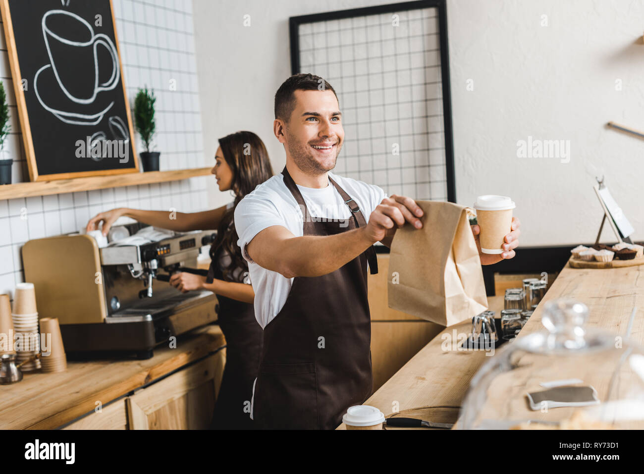 handsome cashier giving paper cup and bag wile barista making coffee ...